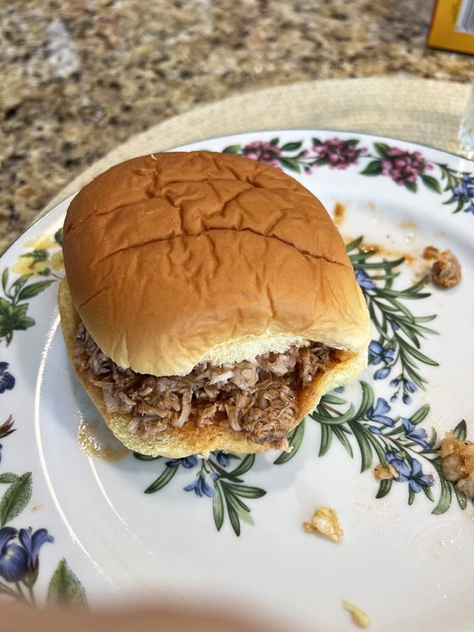 The pulled pork sandwich in its natural habitat&mdash;a soft bun on a floral plate, waiting patiently to change someone's definition of perfection.