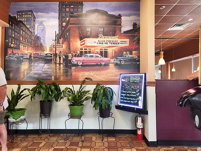 A nostalgic mural of vintage Americana shares wall space with lush plants, reminding us that diners are time machines disguised as restaurants.