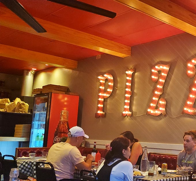 The illuminated PIZZA sign watches over diners like a neon guardian angel, blessing conversations and appetites with its warm, inviting glow.