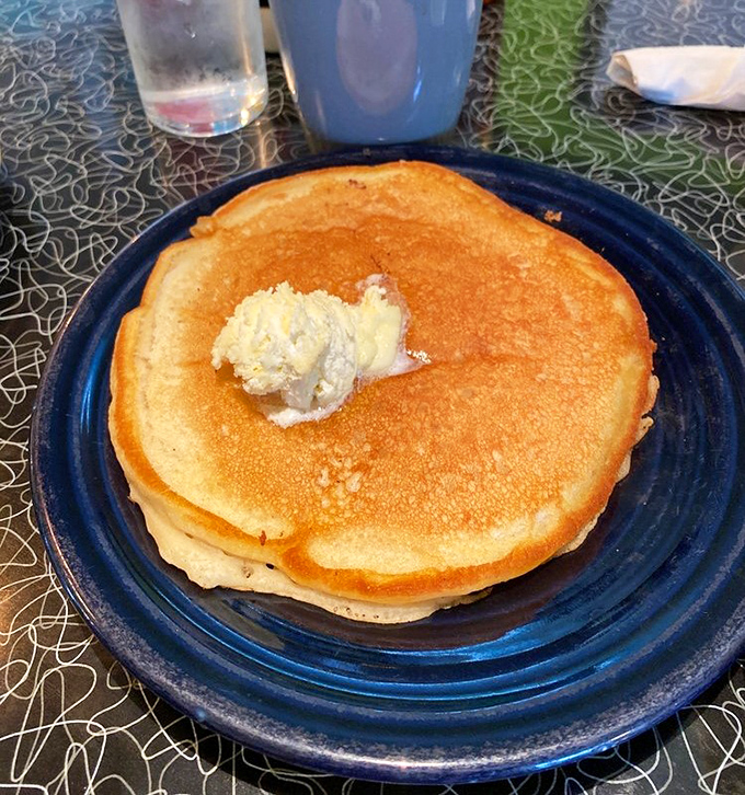 A pancake so perfectly golden it could win a beauty pageant, with a pat of butter slowly melting like a morning sun rising over breakfast mountain. 
