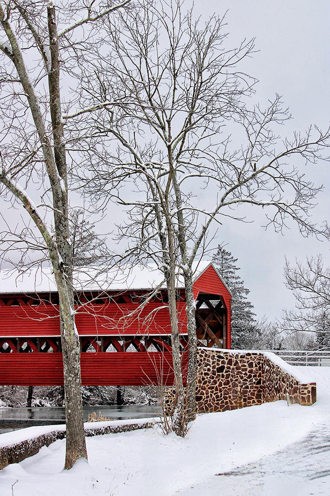 Snow-covered and silent, the bridge stands as a crimson sentinel against winter's white canvas. Those bare trees have witnessed centuries of travelers.