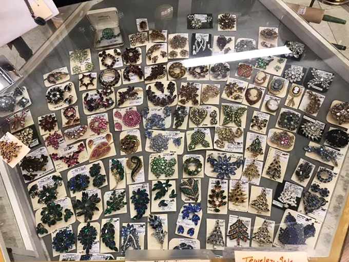 A dazzling constellation of costume jewelry sparkles under glass. Brooches, pins, and earrings arranged like a glittering galaxy of bygone glamour.