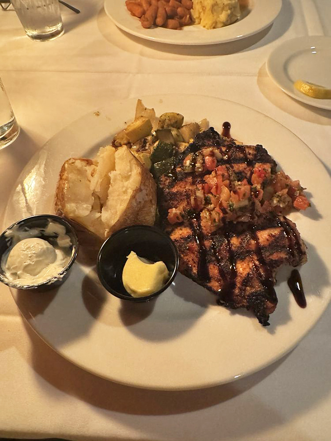 A grilled chicken breast topped with a garden of fresh ingredients, served with a baked potato that's ready for its close-up.