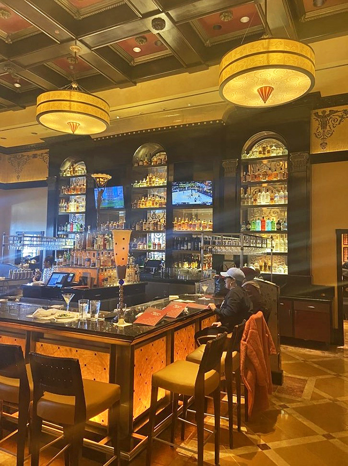 A bar stocked so thoroughly it could survive both apocalypse and prohibition, bathed in amber light that makes everyone look like they belong in a whiskey commercial.