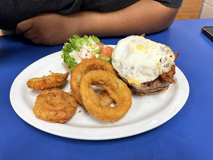 A burger crowned with a sunny-side-up egg, surrounded by golden onion ring sentinels. This isn't just lunch—it's a coronation.