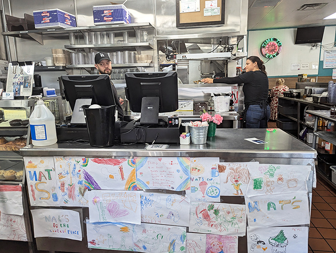 Behind this counter, breakfast miracles happen with clockwork precision. The children's artwork display shows this place has its priorities straight.