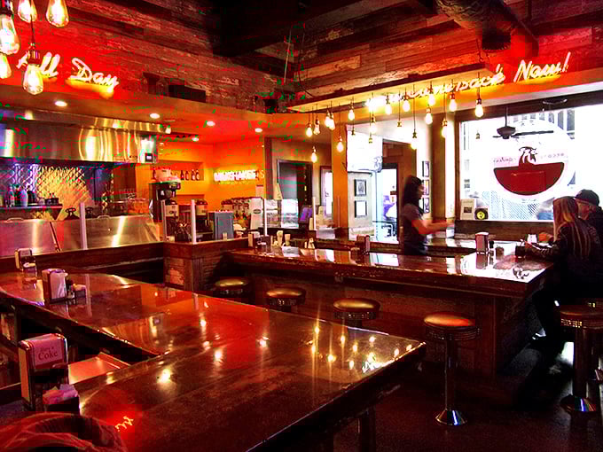 The counter seating offers front-row tickets to the breakfast show. Polished wood reflects the neon glow, creating that classic American diner magic.