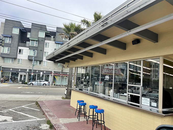 The modern-day diner experience: palm trees, apartment buildings, and blue stools where strangers become friends over shared burger appreciation.