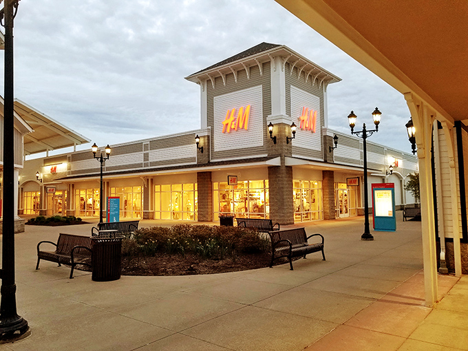 H&M's illuminated storefront stands as a beacon of affordable European style, drawing in shoppers as dusk settles over the outlet center.