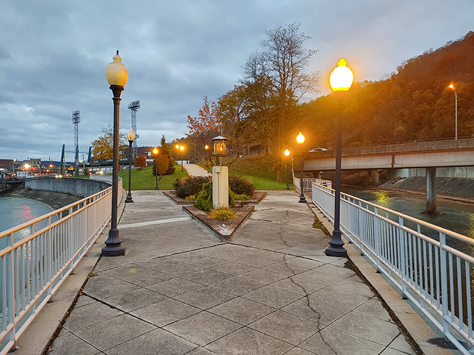 As dusk settles over the riverfront walkway, those glowing lamps create the perfect mood lighting for contemplating both water and steel.