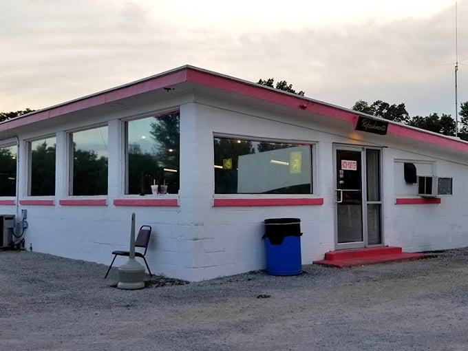 The white and pink concession building glows softly at dusk, beckoning moviegoers with promises of treats and air conditioning between features.