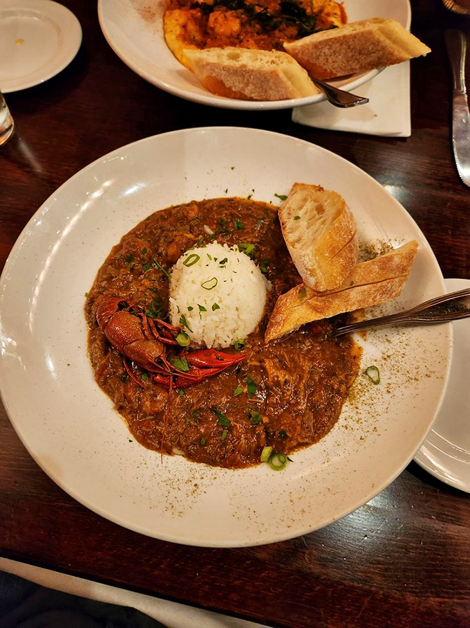 Seafood gumbo dark as a Louisiana night, with rice island rising from the flavorful depths. That crawfish is the exclamation point on a bowl of liquid poetry.