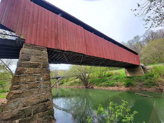 From this angle, you can appreciate how the bridge's rustic red exterior complements the natural stone foundations and emerald waters below.