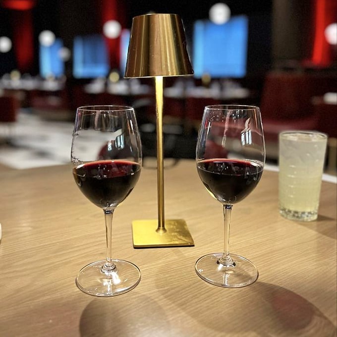 Two glasses of ruby-red wine flanking a gold table lamp&mdash;because at Fahrenheit, even your drinks get mood lighting.