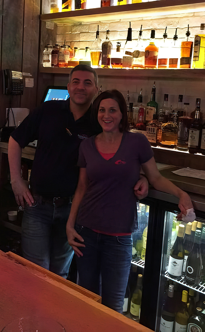 The image shows what appears to be staff members at the bar area, where the backlit bottles create a warm, inviting atmosphere for patrons.