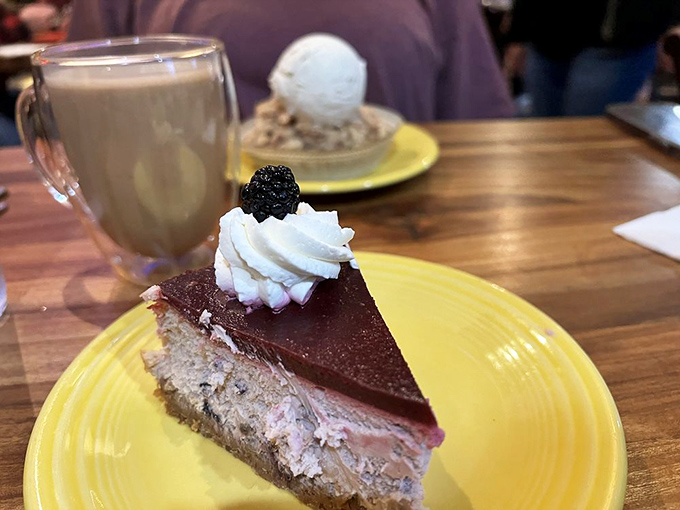 This isn't just cheesecake &ndash; it's a chocolate-topped therapy session on a sunny plate. The blackberry garnish is trying to convince you it's partially fruit salad.