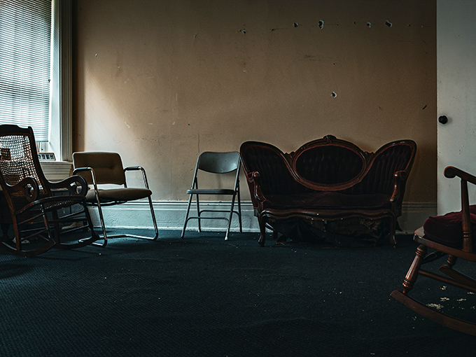 The waiting room where no one waits anymore, these mismatched chairs forming a conversation circle for ghosts to exchange their institutional tales.
