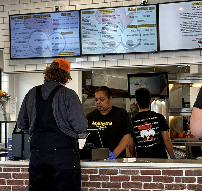 Behind the counter, where fried chicken alchemy happens daily. Those "Mama Knows Best" shirts aren't just cute&mdash;they're stating documented facts.