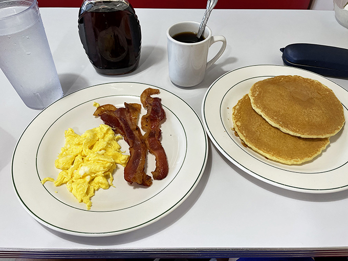 The breakfast trifecta: golden pancakes, scrambled eggs, and bacon strips that have achieved the perfect balance between crispy and chewy.