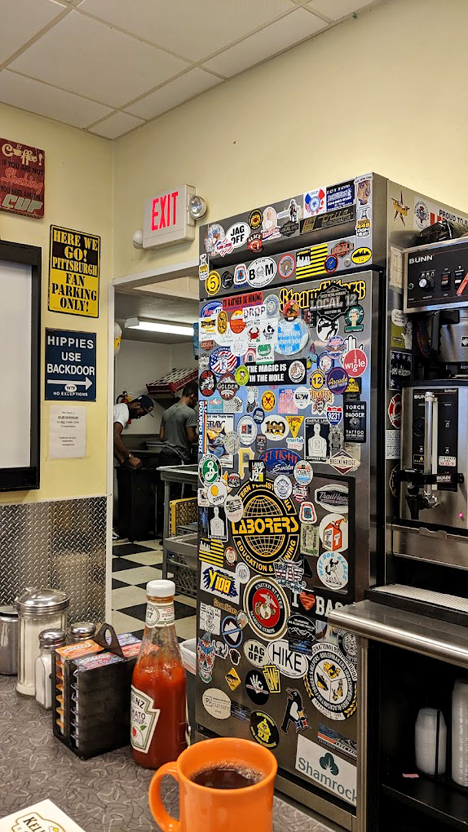 A refrigerator that's earned its stickers like a well-traveled suitcase. "Hippies Use Backdoor" sign is pure diner humor at its finest.
