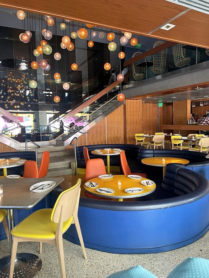 Yellow tables pop against blue banquettes in a color scheme that feels both retro and timeless, like a '60s movie set reimagined for today.