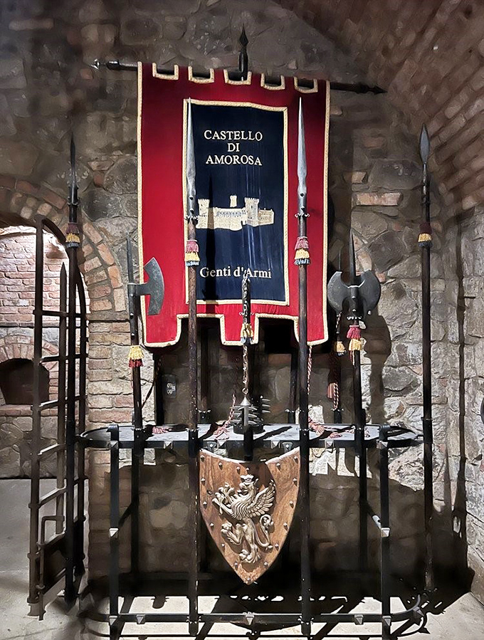 Medieval weaponry and a heraldic banner stand ready behind iron bars, protecting visitors from impulse purchases of historically accurate battle axes.