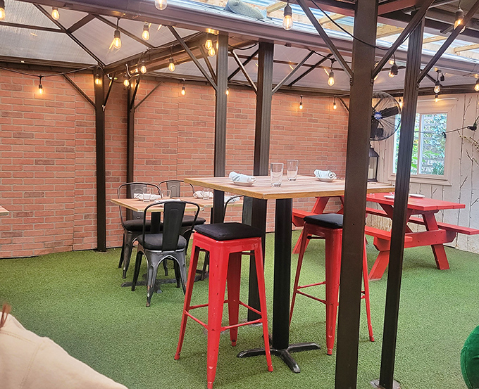 The covered patio with its string lights and brick walls creates an urban oasis where red stools pop against the industrial backdrop.