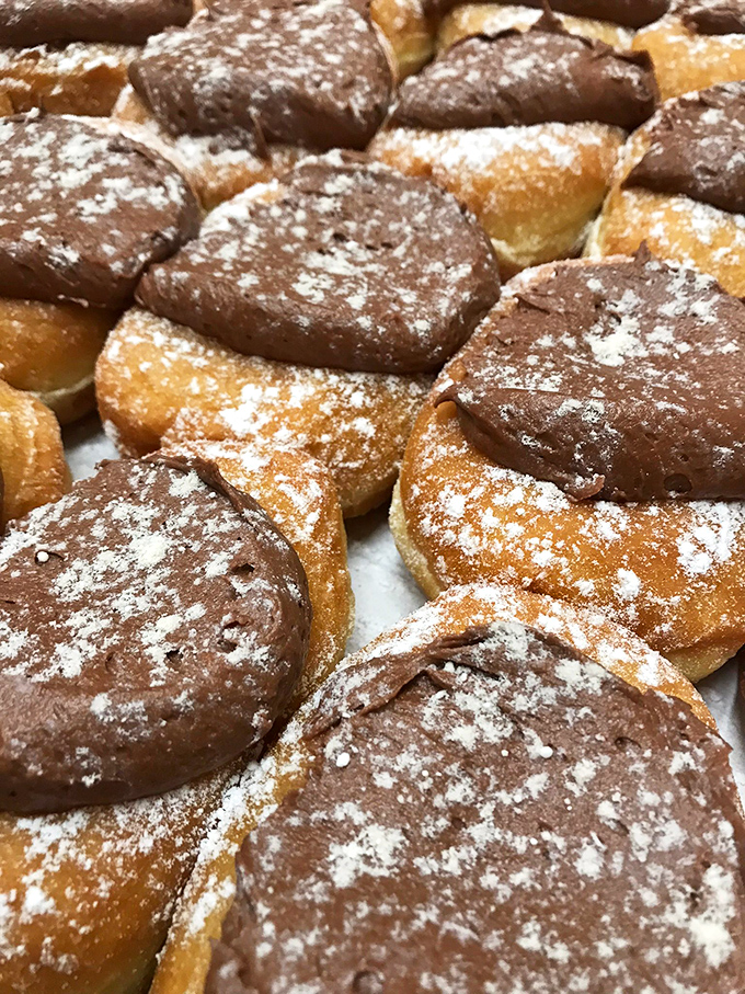 Powdered sugar dusts these chocolate-topped treasures like fresh snow, hiding custard centers that surprise with every bite.