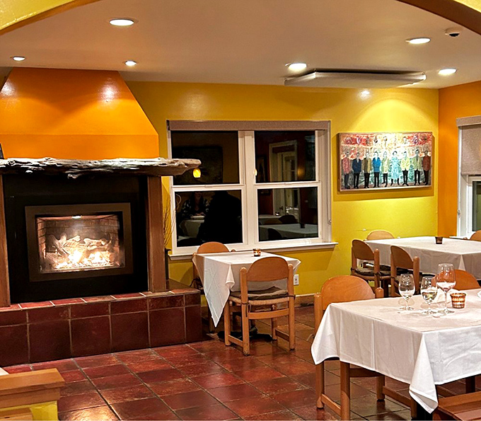 The fireplace corner &ndash; where comfort food meets actual comfort. Nothing says "stay awhile" like terra cotta floors and warm yellow walls.