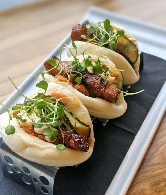 Steamed buns cradle tender meat like soft clouds holding delicious secrets, garnished with microgreens that add both color and conscience.