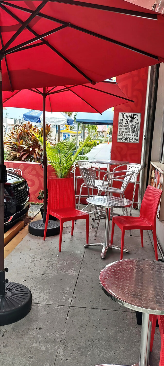 Miami sunshine filters through red umbrellas, creating the perfect outdoor setting for savoring fritas while watching the world go by.
