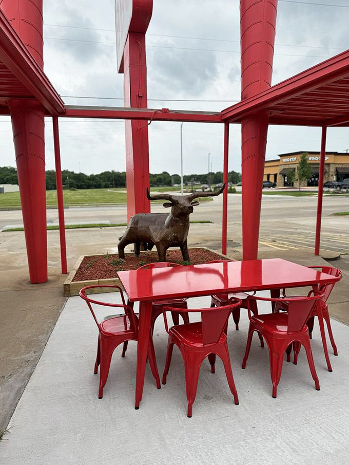Outdoor seating with a metal bull sculpture &ndash; because nothing says "Texas barbecue" quite like dining under red awnings with livestock art.