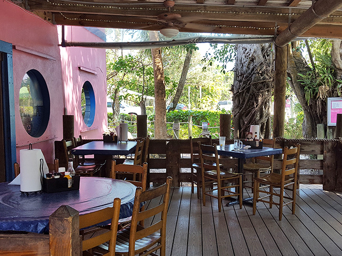 Outdoor seating that captures the essence of island dining&mdash;casual wooden chairs, tropical foliage, and that pink wall providing the perfect backdrop.