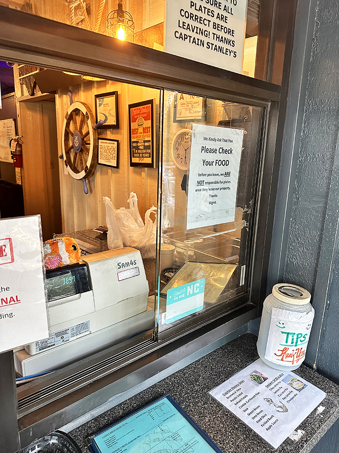 The takeout counter speaks volumes: handwritten specials, a ship's wheel, and a tip jar—the holy trinity of authentic seafood joints.