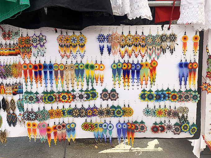 Beaded earrings dance in the sunlight, their vibrant patterns and colors transforming a simple white display into a mesmerizing gallery of wearable art.
