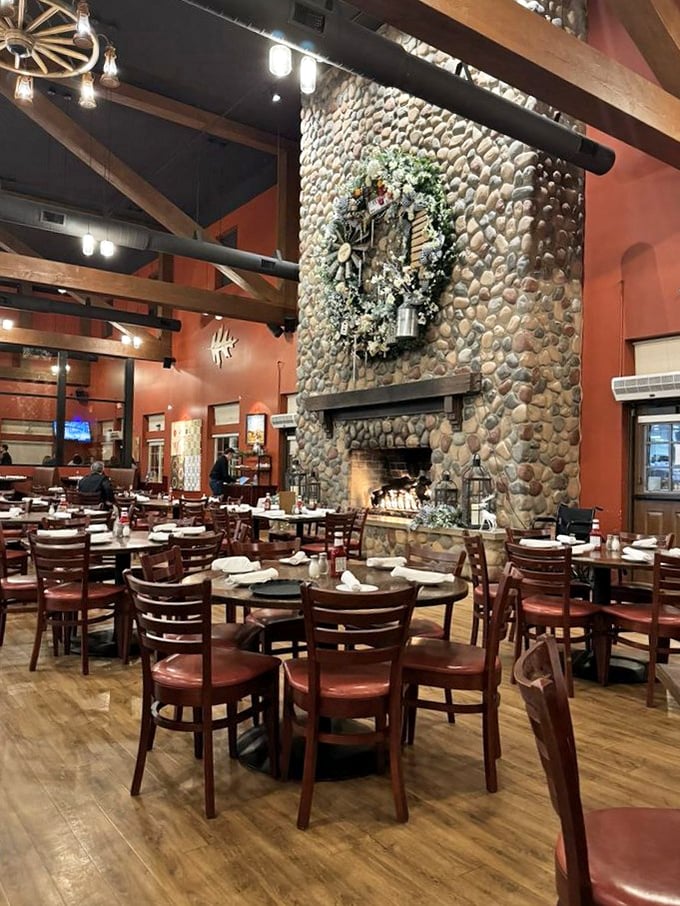 The massive stone fireplace anchors the dining room like a rustic cathedral, drawing the eye upward to soaring wooden beams.