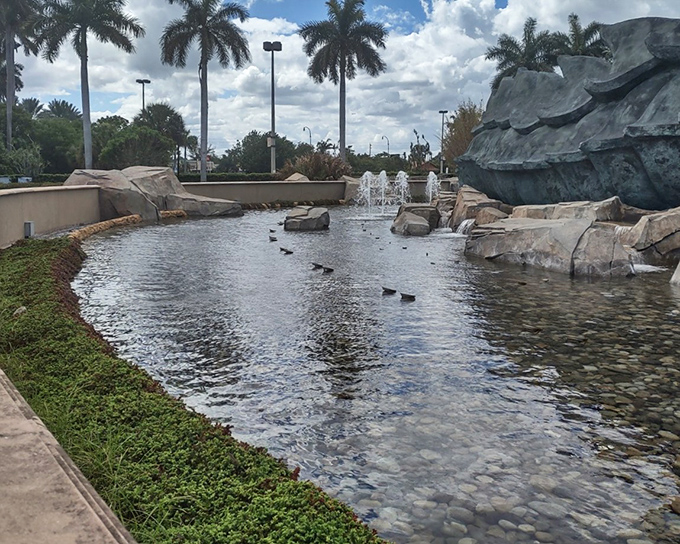 A tranquil reflecting pool surrounds the base of the statue, where real ducks swim beneath mythological beasts.