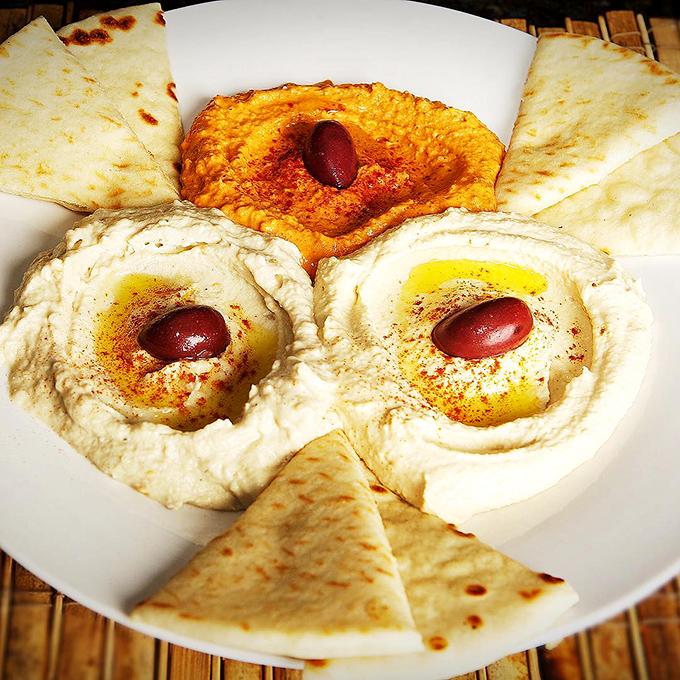 Hummus trio with kalamata olives standing guard&mdash;creamy, dreamy chickpea perfection that makes store-bought versions hide in shame.
