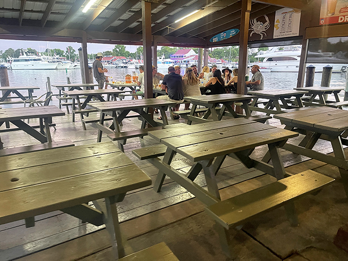 Picnic tables under a covered deck offer front-row seats to nature's aquatic theater, with boats and birds providing the entertainment.