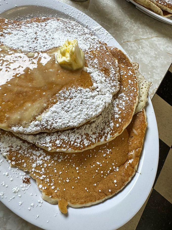 Pancakes so perfectly golden they deserve their own Instagram filter, dusted with powdered sugar like fresh snow on Christmas morning.