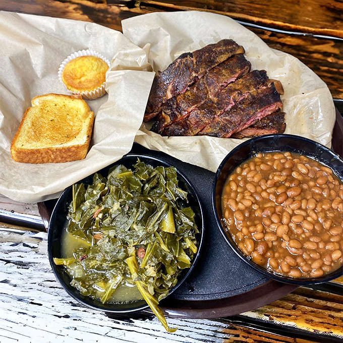 The barbecue trinity: smoke-kissed meat, collards cooked to silky submission, and beans that have clearly been simmering since breakfast, all served with cornbread that needs no introduction.