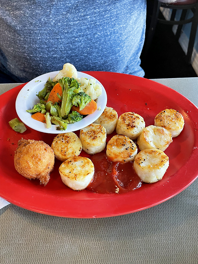 Perfectly seared scallops with a side of vibrant vegetables prove that simple preparation lets quality ingredients shine. That single hush puppy is the chef's exclamation point. 