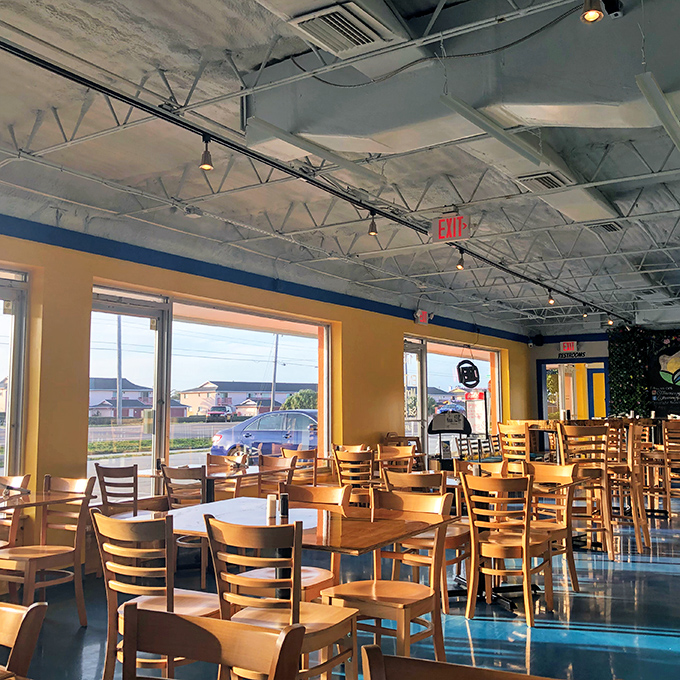 Sun streams through large windows, illuminating wooden chairs waiting for the breakfast crowd. The industrial ceiling adds just enough edge to the cozy vibe.