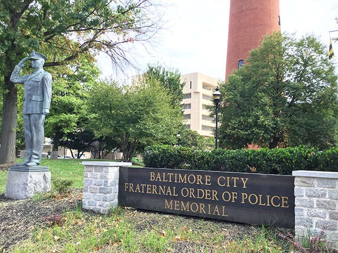 The Police Memorial stands in solemn contrast to the industrial tower behind it. Different purposes, different eras, united in their Baltimore legacy.
