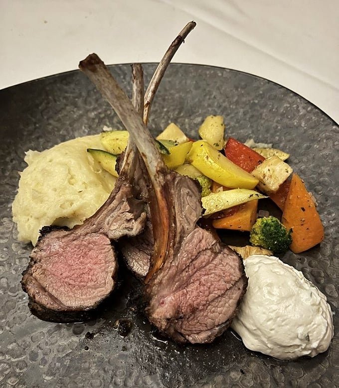 Lamb chops standing at attention like meaty sentinels, pink-centered and perfect, surrounded by a rainbow of roasted vegetables.