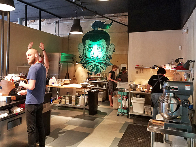 The open kitchen, complete with a watchful neon guardian, invites diners into the controlled chaos where brunch dreams are made real.