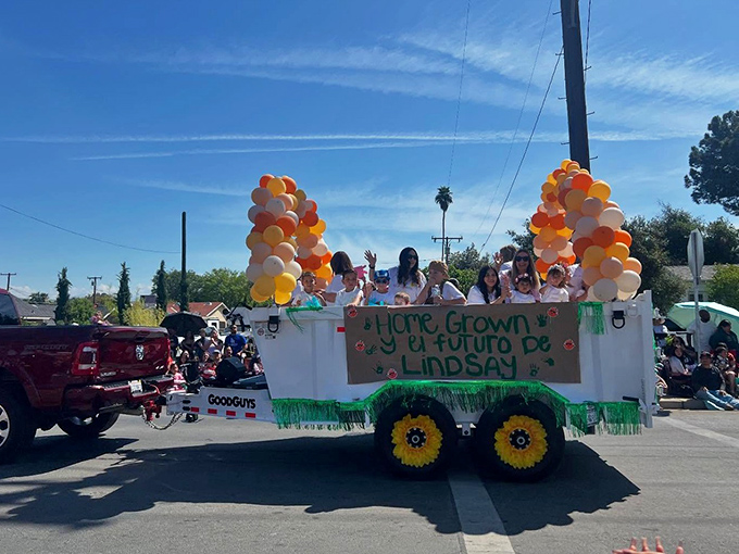"Home Grown y el futuro de Lindsay"&mdash;parade floats celebrate the town's agricultural heritage and its bright, balloon-decorated future.
