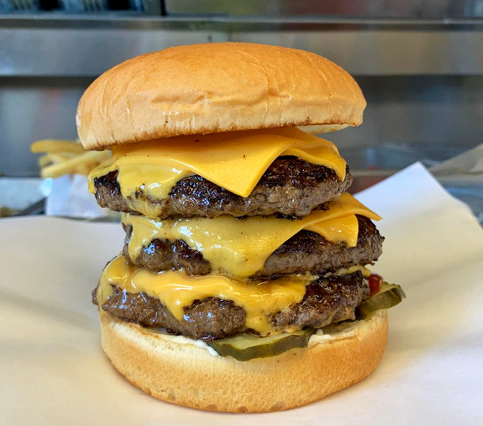 The triple-decker that dares you to unhinge your jaw. More cheese than a 1980s rom-com and worth every napkin you'll need.