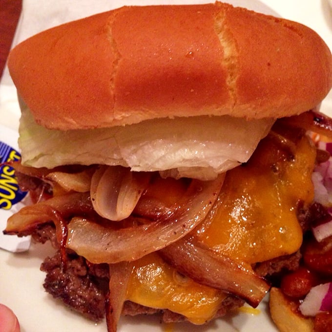 A burger that requires jaw exercises before attempting. Melted cheese cascades over the patty like a golden waterfall.