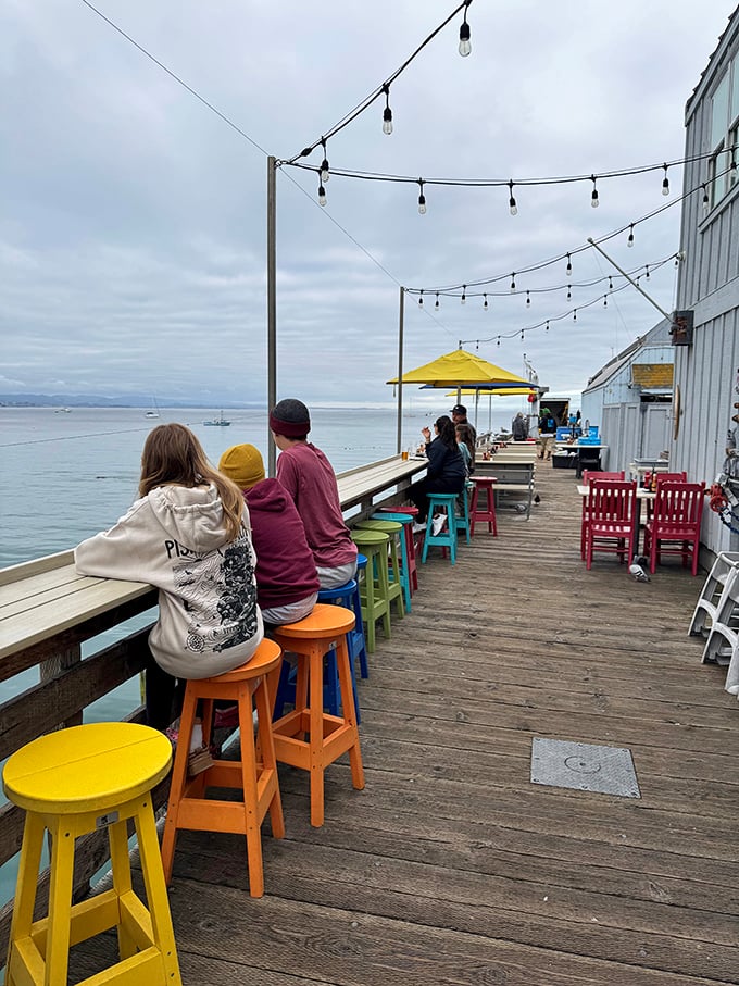 Outdoor seating with colorful stools adds a playful touch to pier dining – string lights included for maximum coastal charm.